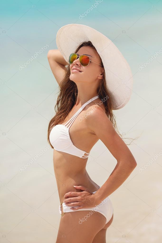 Hermosa mujer en bikini blanco y sombrero en una playa tropical . — Foto de stock #64128717 © golyak