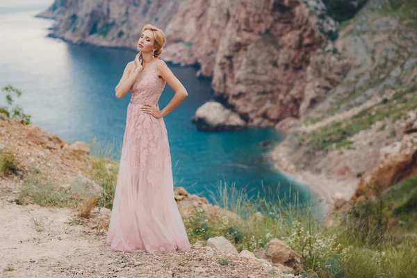 Bride in wedding dress stands on a cliff with a beautiful sea view from ...