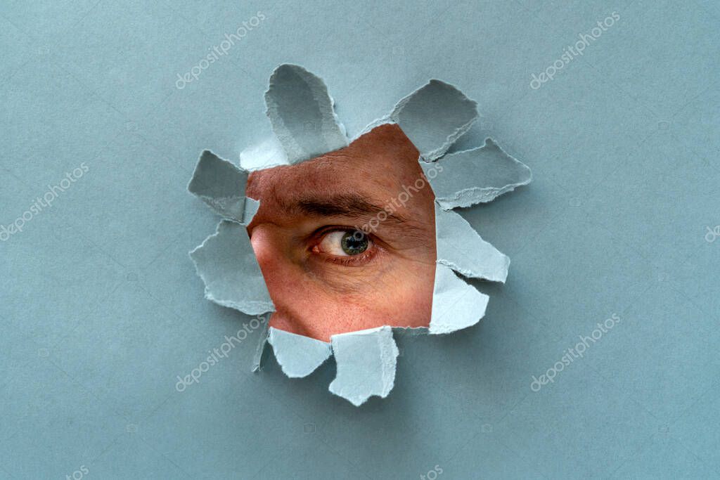 El ojo humano nos observa a través de un agujero en un papel gris 2024