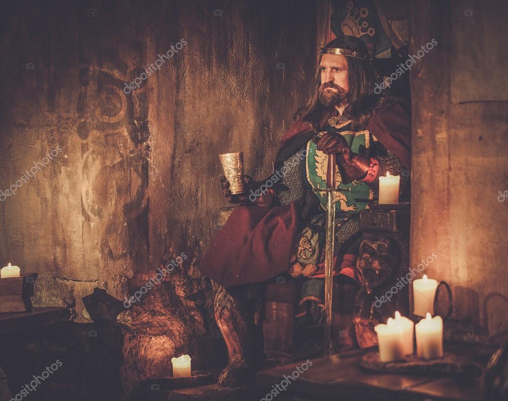 Old medieval king with goblet of wine on the throne in ancient castle ...