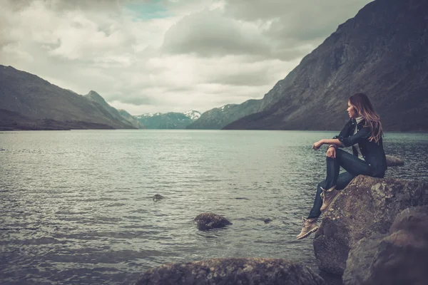 Beautiful woman posing on the shore of a wild lake, with mountains on ...