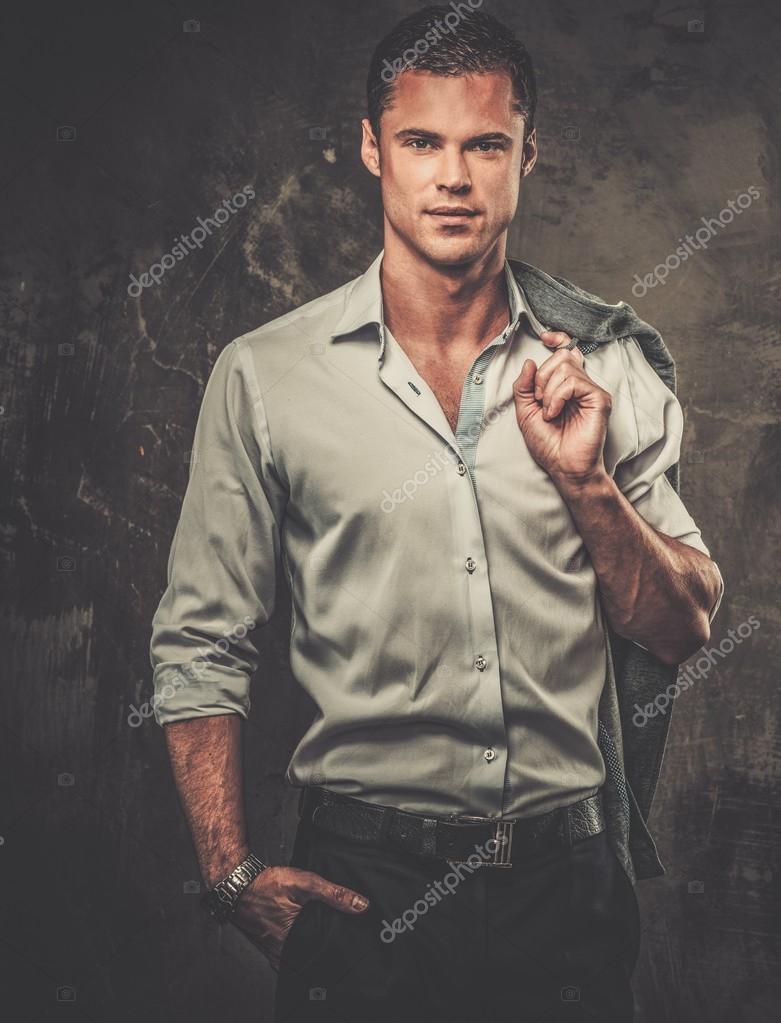 Handsome man in shirt against grunge wall holding jacket over shoulder ...