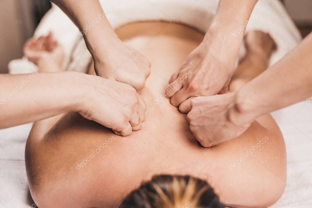 El masaje de espalda en cuatro manos simultáneamente - dos masajistas profesionales que tratan ...