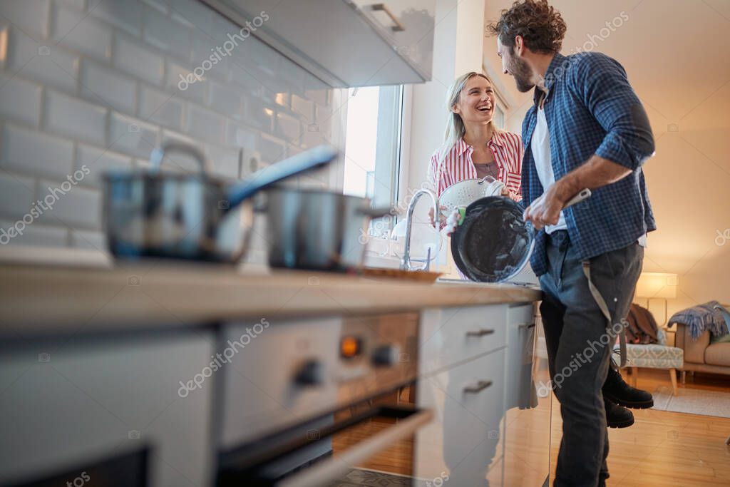 Una joven pareja haciendo quehaceres domésticos con satisfacción en un ambiente alegre. Cocina ...