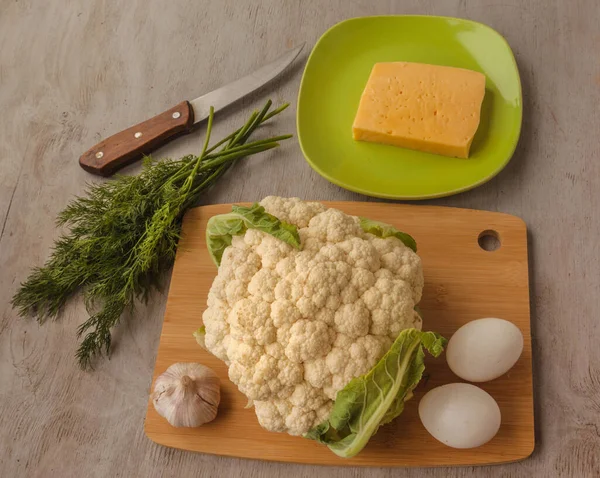 Una cabeza de coliflor y otros productos en una tabla de cortar junto a ...