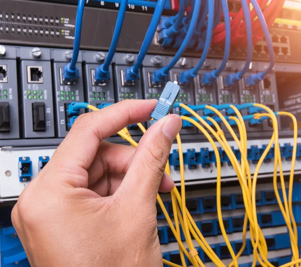 man working in network server room with fiber optic hub for digital ...