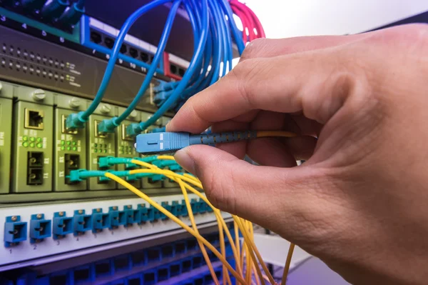 man working in network server room with fiber optic hub for digital ...