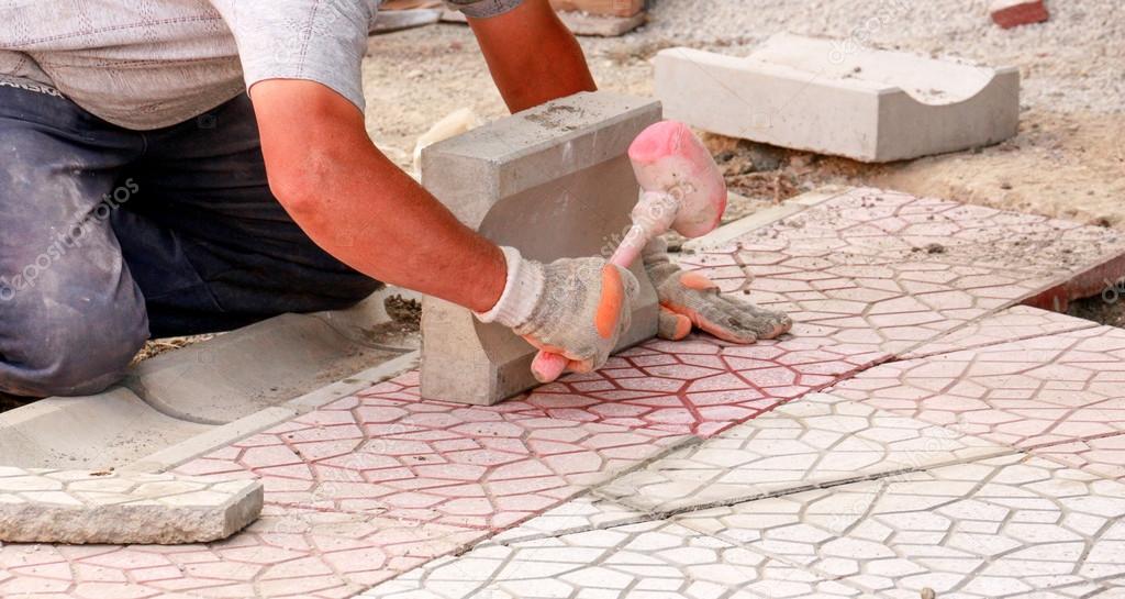 Workers tapping pavers into place with rubber mallets. Installation of ...