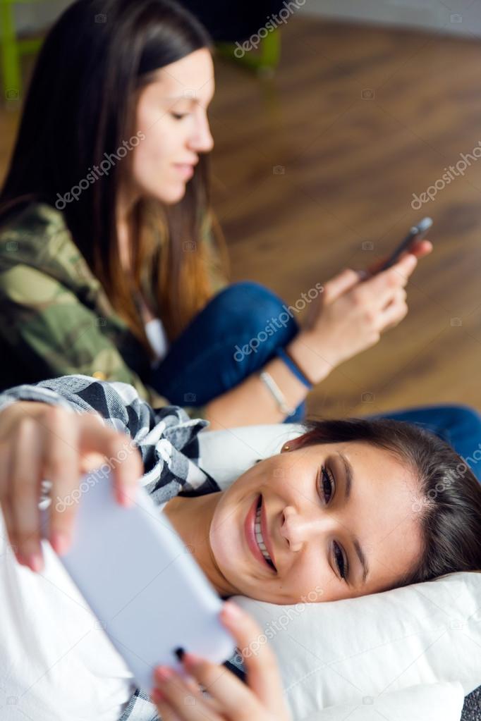 Two beautiful young woman using mobile phone at home. — Stock Photo ...