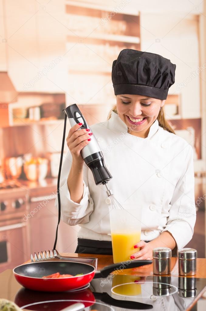 Woman chef wearing full cooking outfit standing using electric blender ...