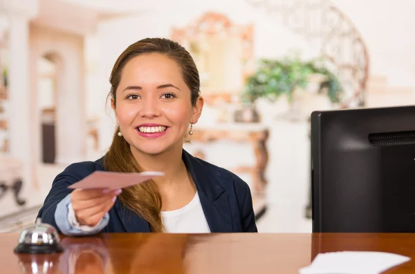 Young brunette hotel receptionist with friendly smile handing over key ...