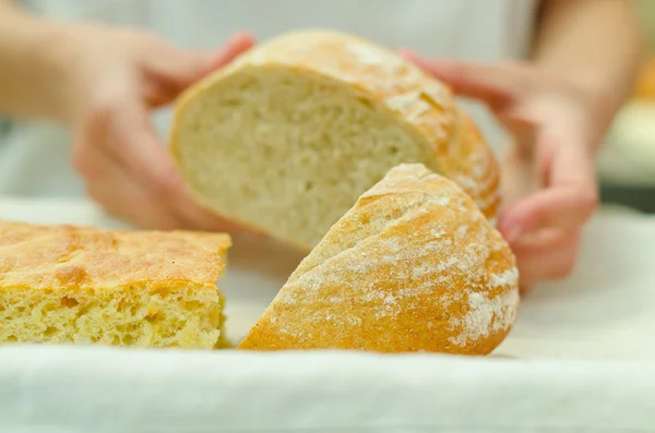 Bakers hands placing half cut loaf of bread onto white plate next to ...