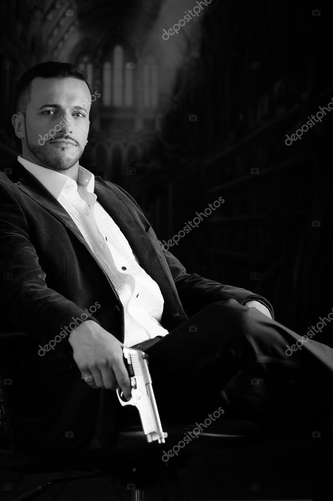 Elegant man sitting in a chair holding gun over dark background — Stock ...