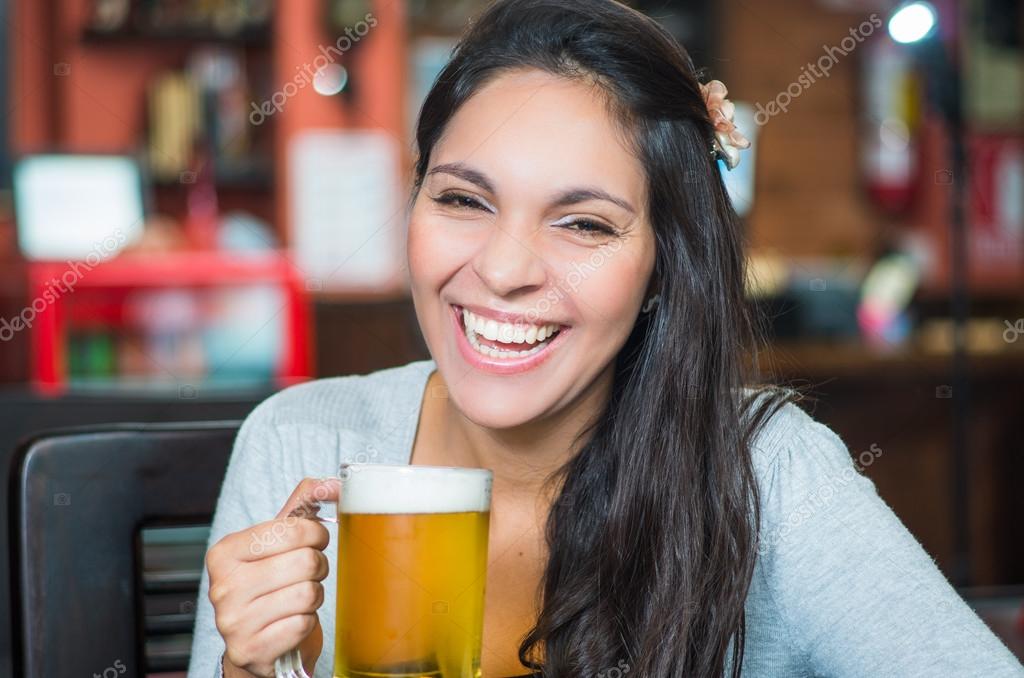 Brunette model sitting by restaurant table holding glass of beer and ...