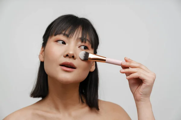 Asian Shirtless Woman Using Powder Brush While Doing Makeup Isolated