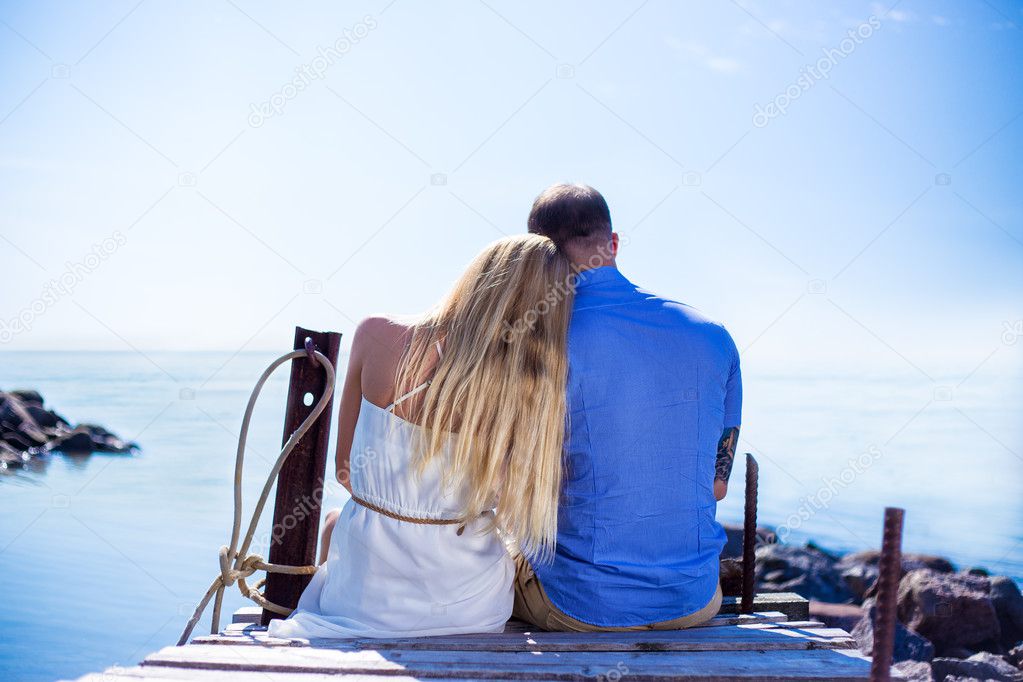 Back view of romantic young couple sitting on the pier Stock Photo by ...