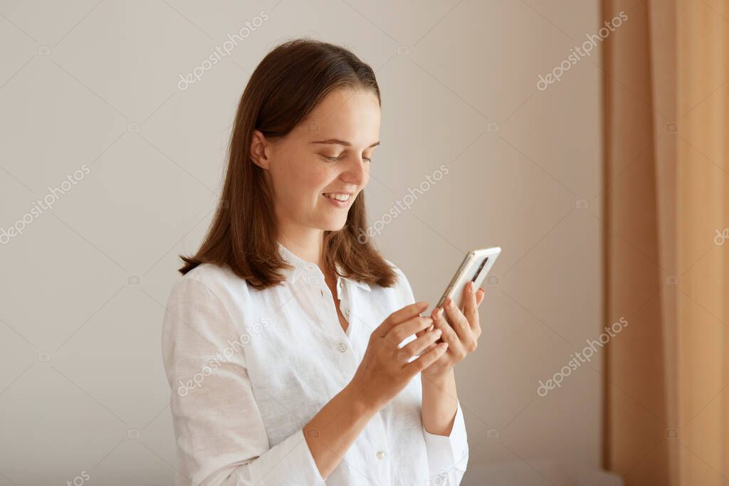 Foto interior de hermosa mujer morena sonriente con camisa de algod n blanco usando tel fono m ...