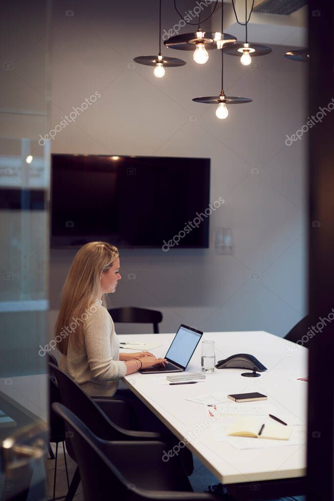 Empresaria que trabaja tarde en la sala de reuniones de la oficina usando el ordenador portátil 2024