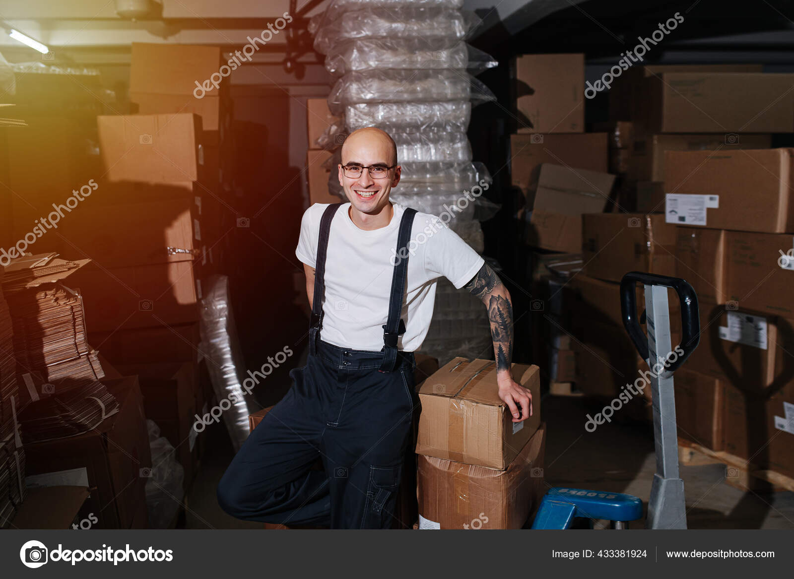Charming male warehouse worker leaning on stack of carton boxes on ...