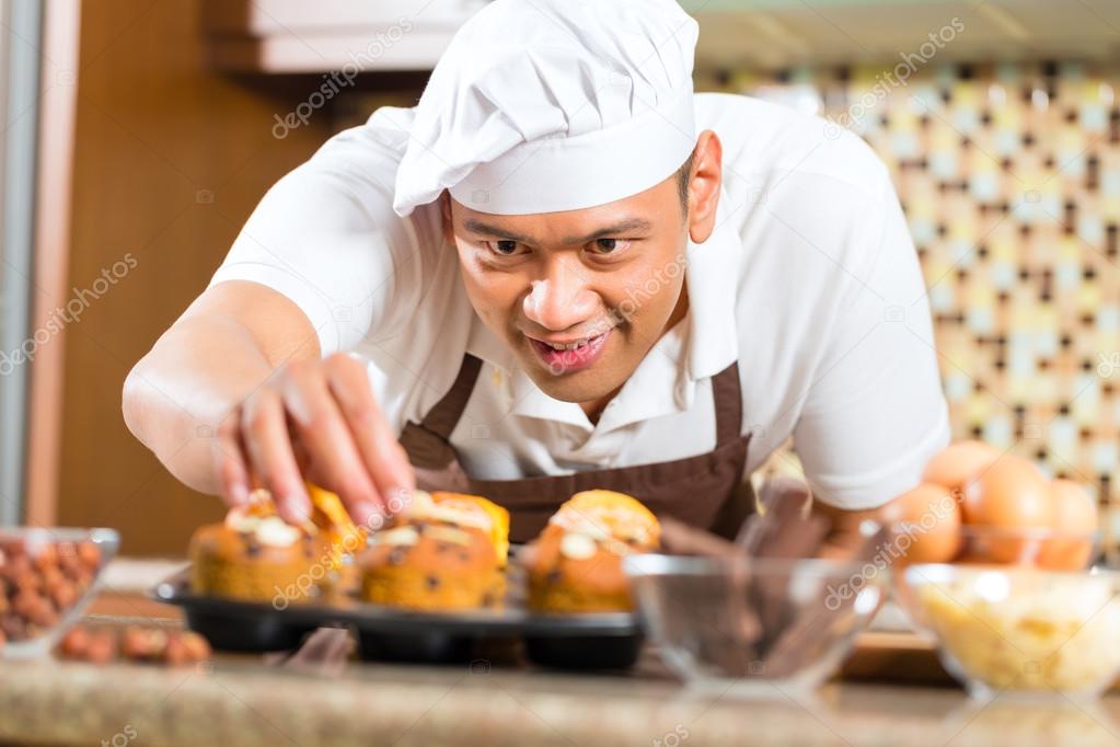 Asian man baking muffins in home kitchen — Stock Photo © Kzenon #81962146