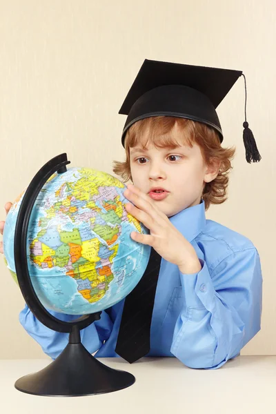 Little professor in academic hat looks at globe - Stock Image - Everypixel