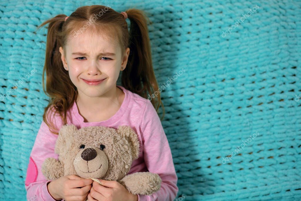 Triste bebé llorando sentado en el sofá azul y abrazando a su osito de ...