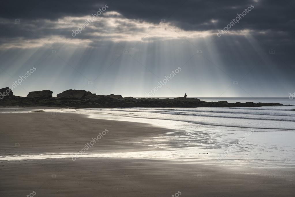 Stunning sun rays bursting from sky over empty yellow sand beach ...