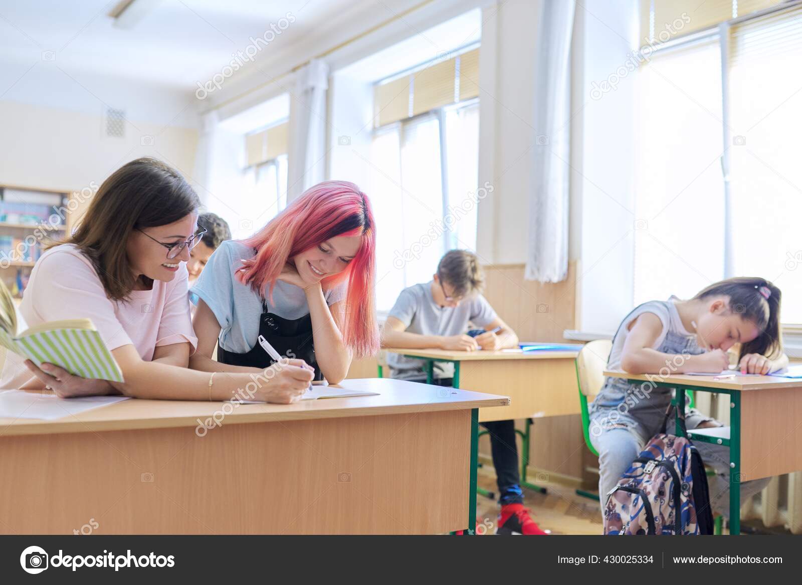Lesson in class of high school students, female teacher sitting at desk ...