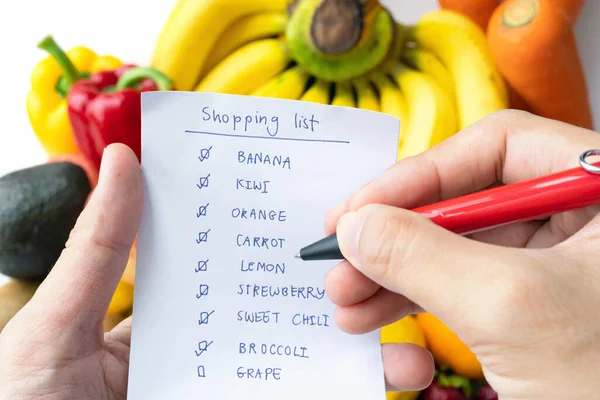 Hands hold shopping list checking with variety of colorful fresh fruits ...