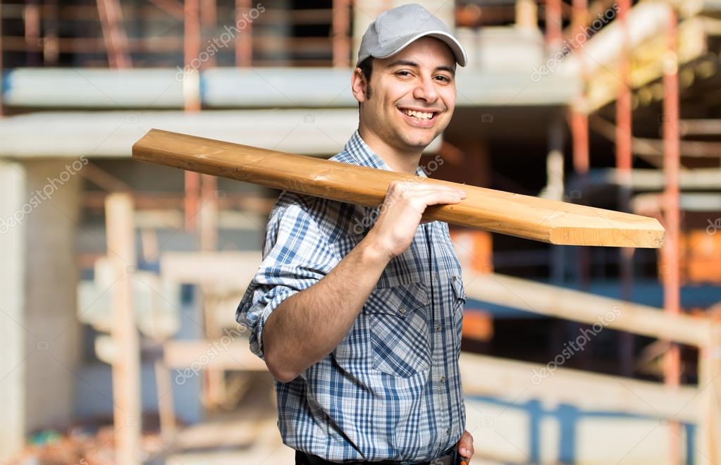 Smiling carpenter holding wood plank Stock Photo by ©minervastock 70777369