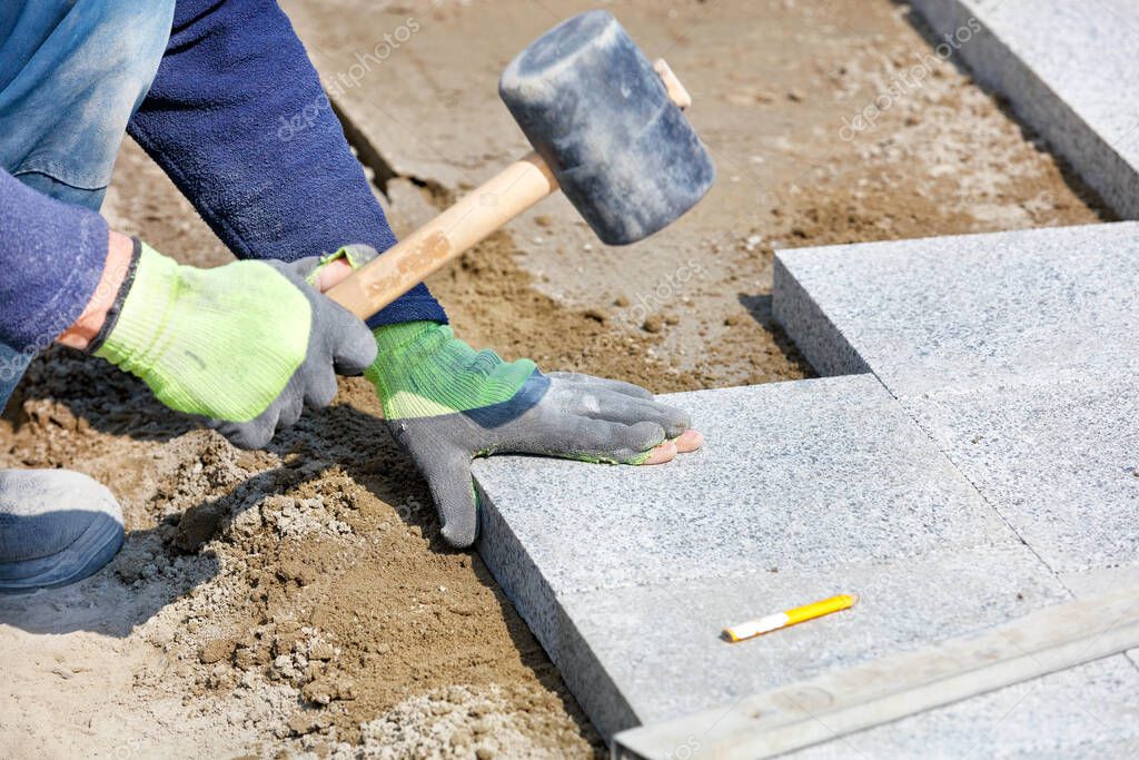 Un trabajador con un mono azul, medio agachado, golpea con un martillo ...
