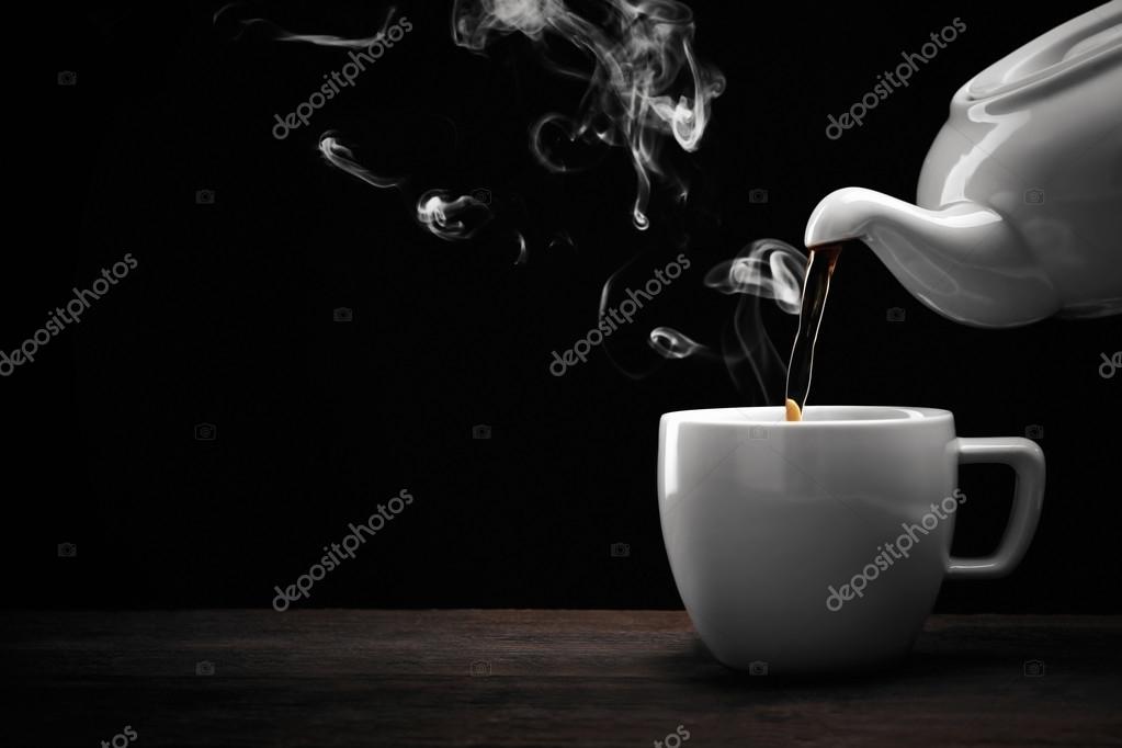 Pouring hot tea from a kettle into a cup on black background, close up ...