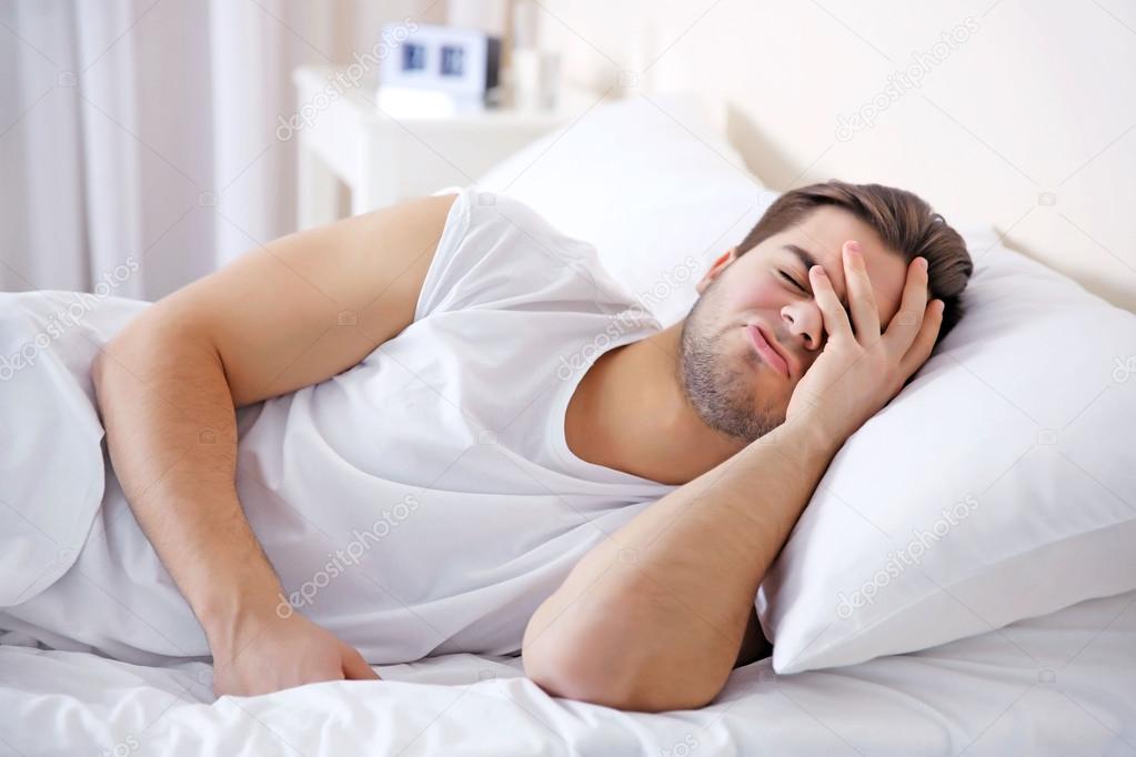 Young man lying in bed at home Stock Photo by ©belchonock 101671284