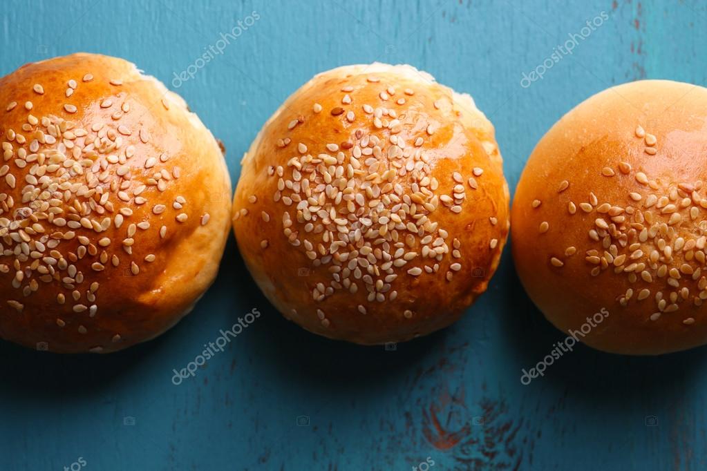 Tasty buns with sesame on color wooden background Stock Photo by ...