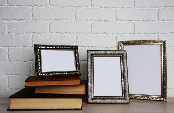 Golden photo frames with books on wooden surface, on brick wall ...