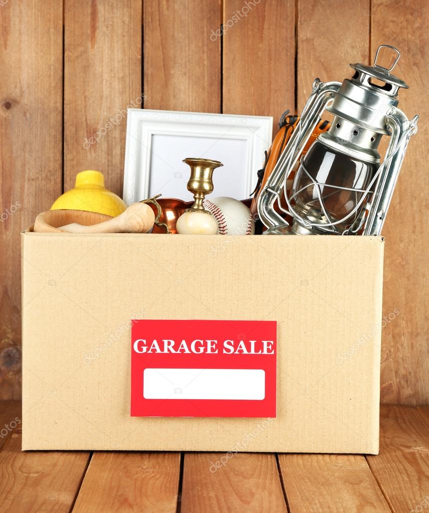 Box of unwanted stuff ready for a garage sale on wooden background ...
