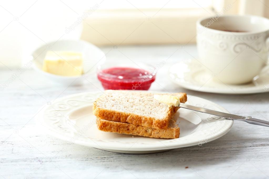 Toasts with butter on plate with cup of tea on light background Stock ...