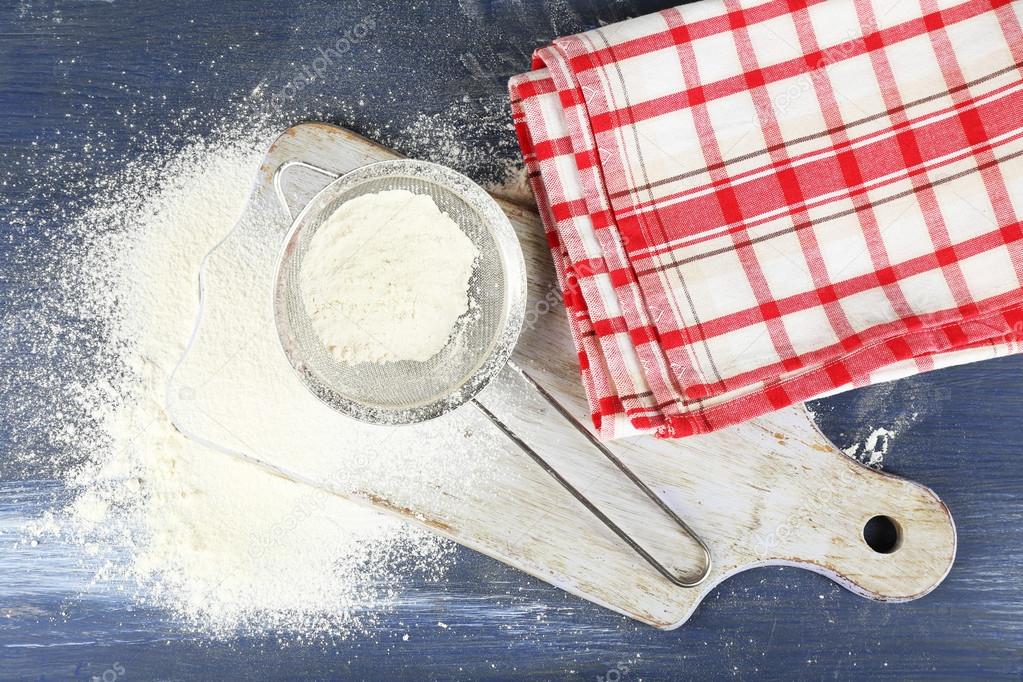 Sifting flour through sieve on cutting board and on wooden table, top ...