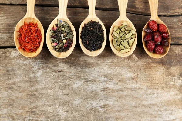 Collection of tea and natural additives in wooden spoons, on old wooden ...