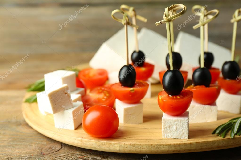 Cheese canapes with cherry tomatoes and olives on wooden tray close up ...