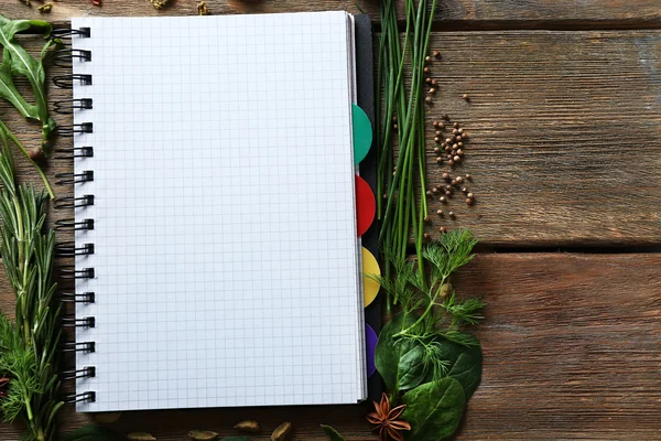 Open recipe book with fresh herbs and spices on wooden background ...
