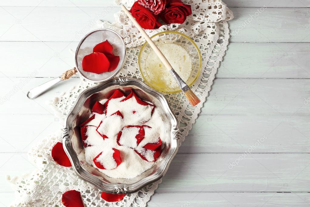 Making candied rose flower petals with egg whites and sugar, on wooden ...