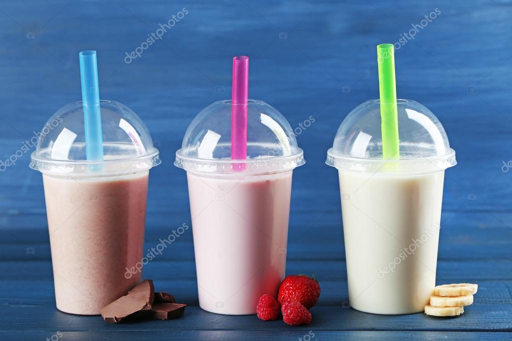 Plastic cups of milkshake on color wooden background Stock Photo by ...