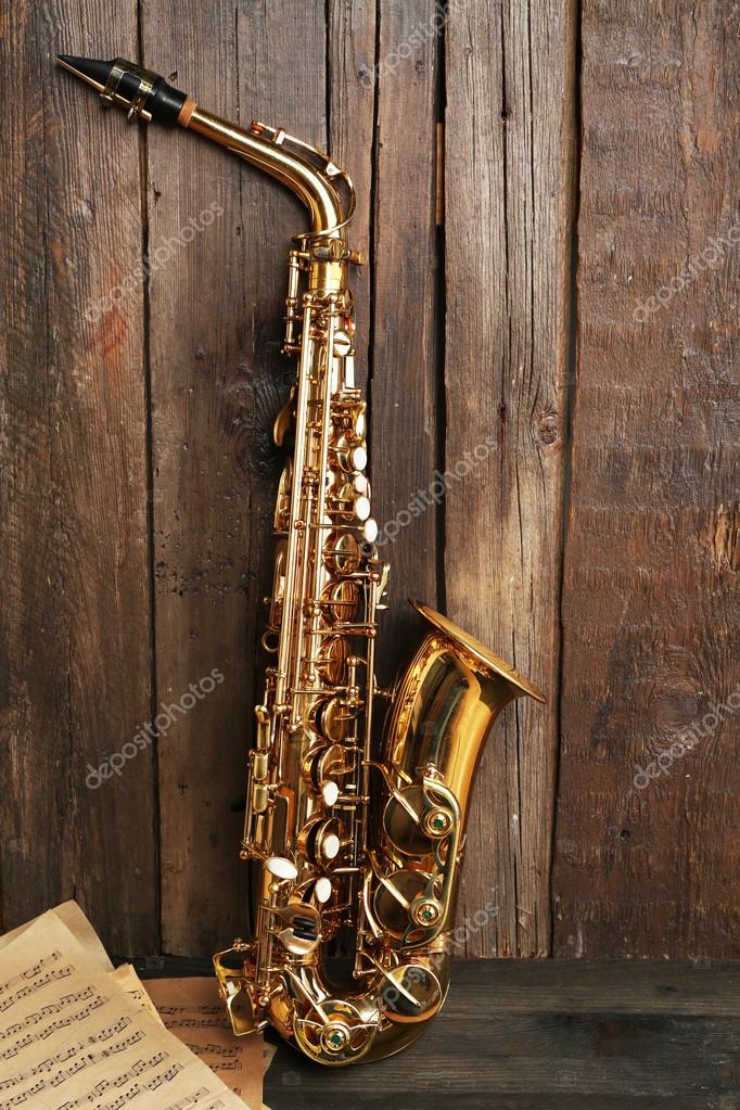 Beautiful golden saxophone with musical notes on wooden background ...