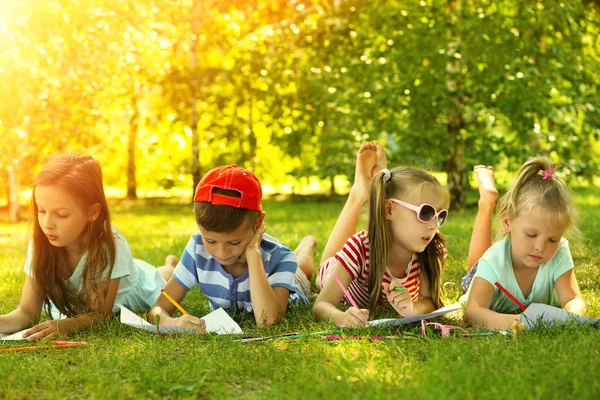 Happy active children lying on green grass and drawing in park Stock ...