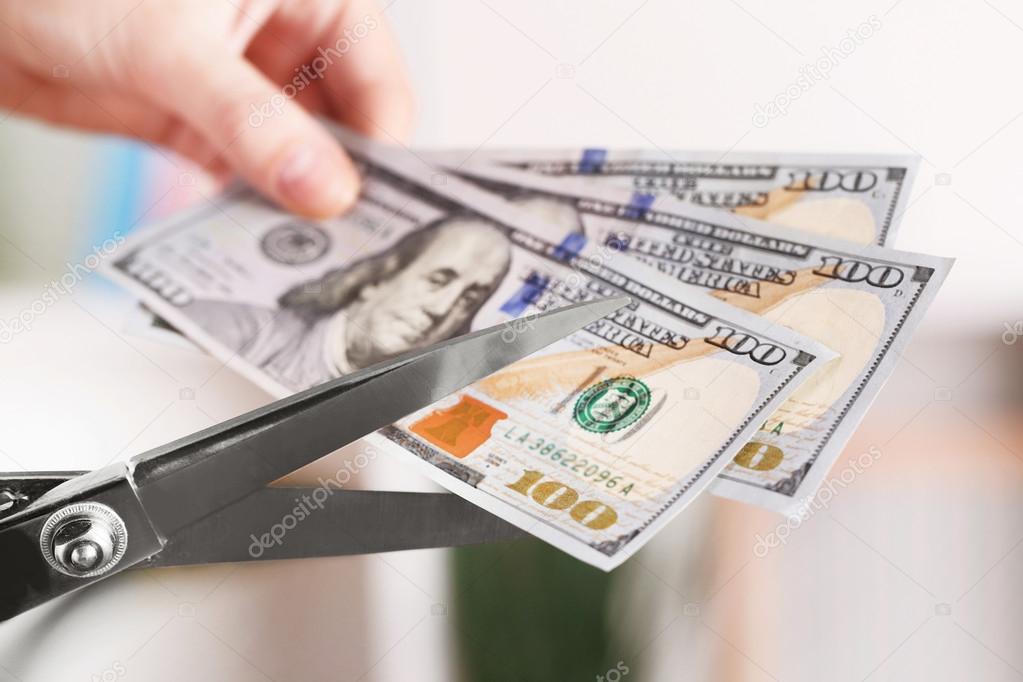 Hands with scissors cutting dollar banknotes, on blurred interior ...