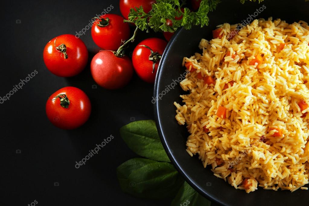 Stewed rice with a carrot and tomatoes on a plate over black background ...