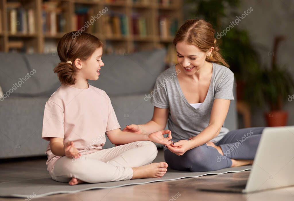 Joven mamá positiva mostrando linda hija pequeña cómo meditar mientras ...