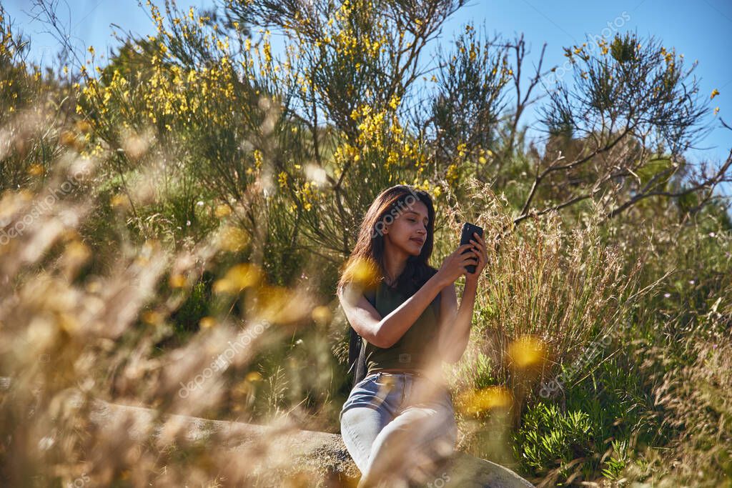 Jovencita absorta sentada en una roca enviando mensajes de texto con ...