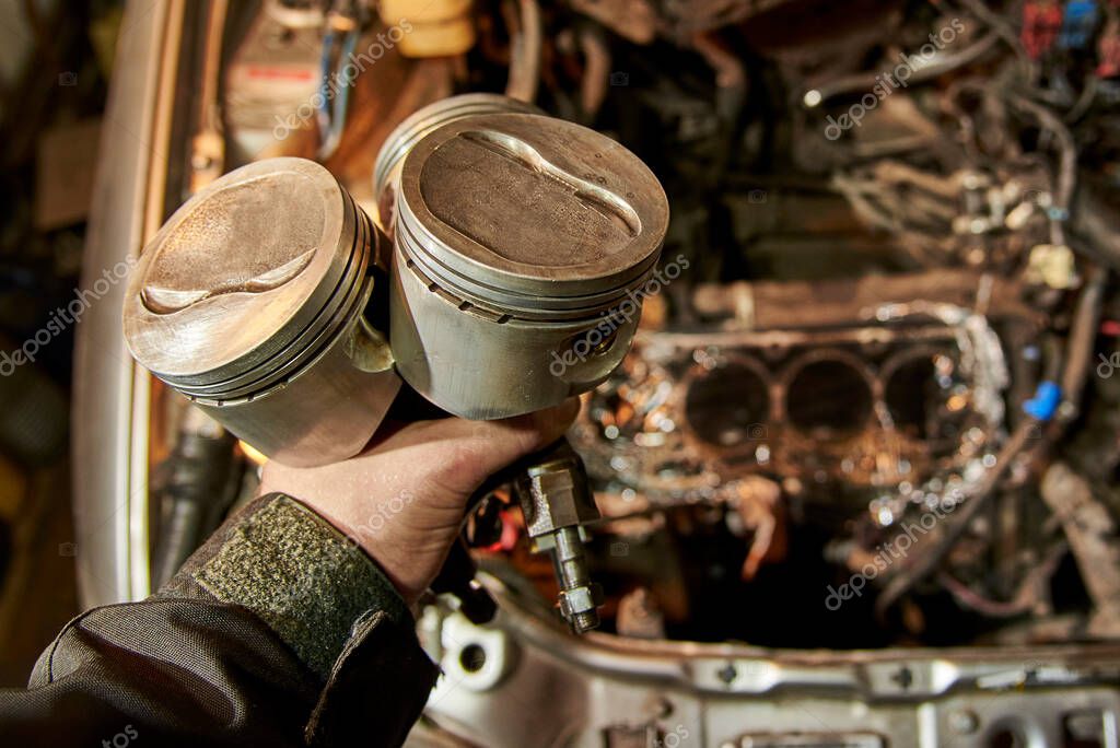 Un hombre sostiene un pistón de un coche contra el fondo de un motor ...